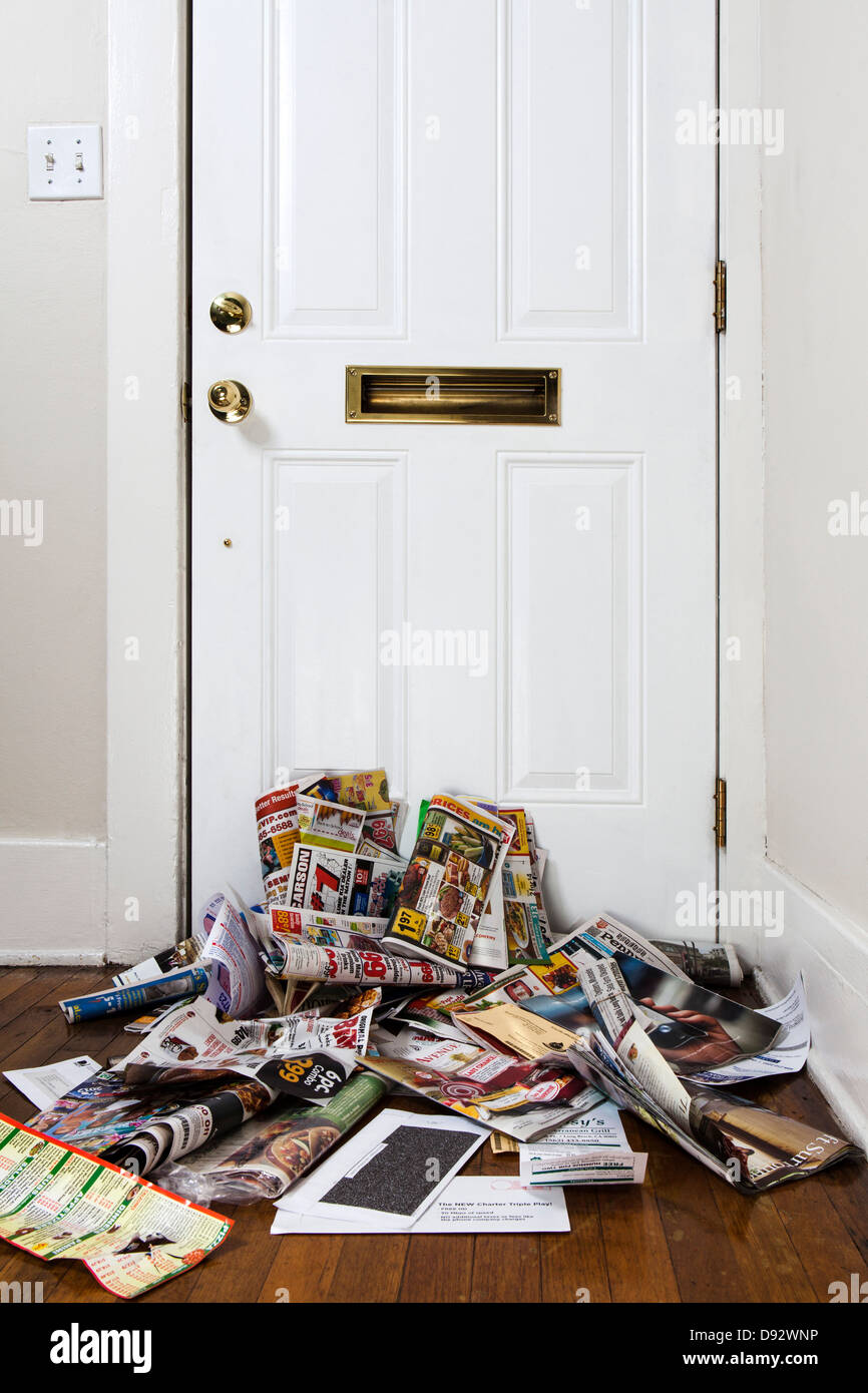 A heap of mail and newspapers under a mail slot in a home entrance hall ...