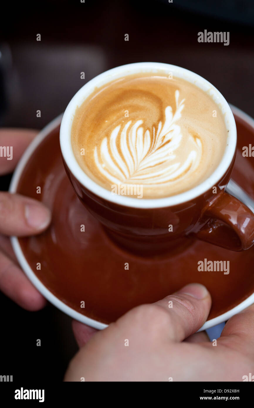 A barista serving a cappuccino with a floral pattern in the milk froth ...