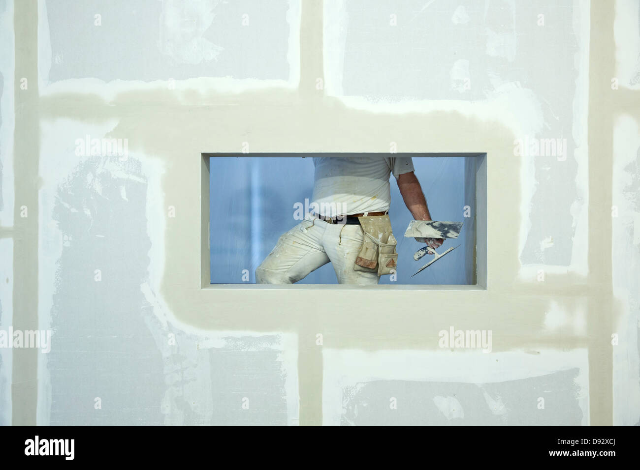 A house painter holding a trowel, seen through window hole in a newly ...