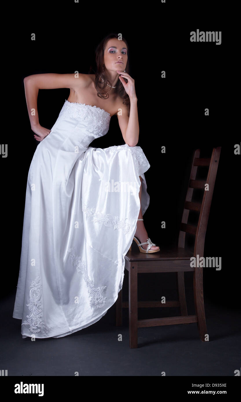 beatiful young woman in wedding dress on black stands with one leg on a ...