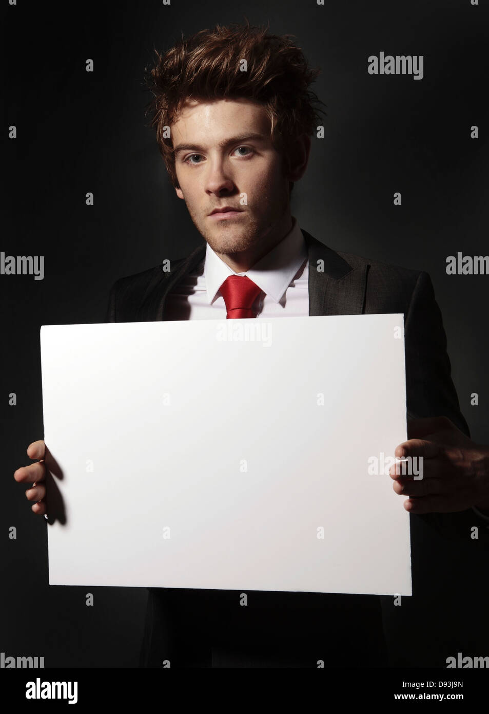 low key portrait of a young man in a suit hold a white card Stock Photo ...