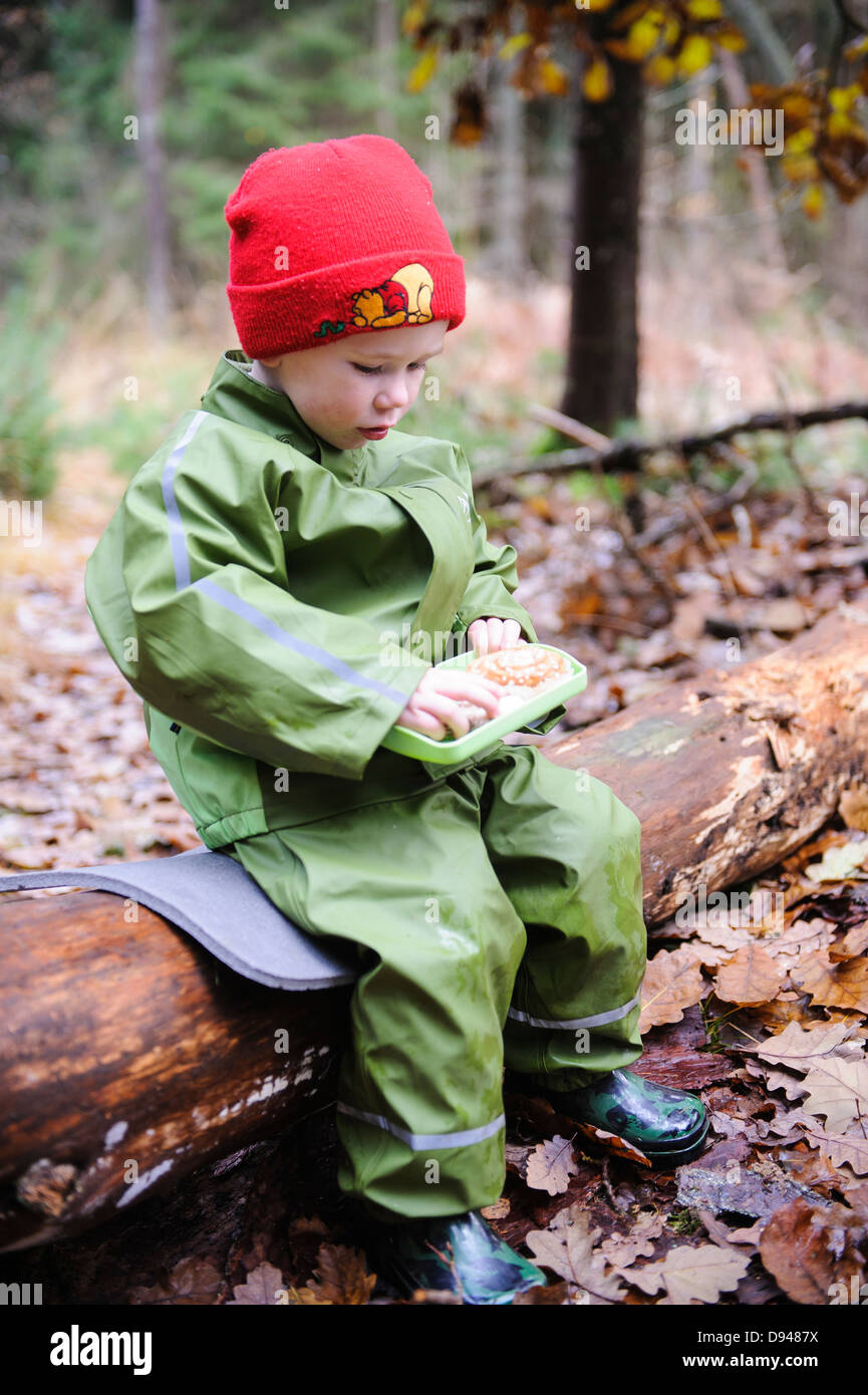 Boy sitting on log and eating Stock Photo - Alamy
