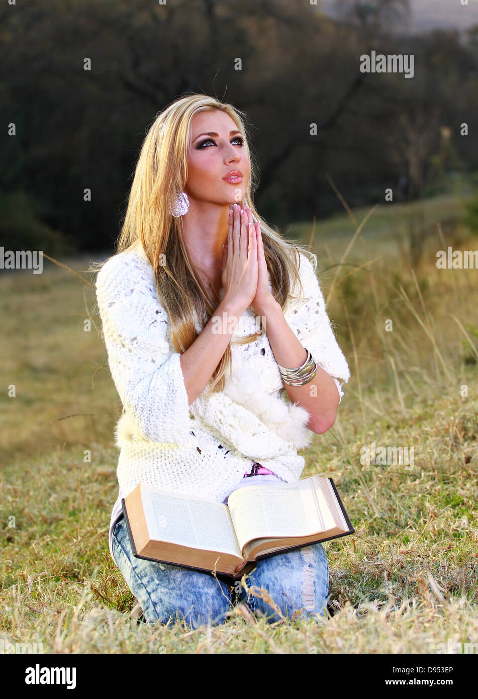 A young blond lady is sitting on her knees, kneeling and praying with ...