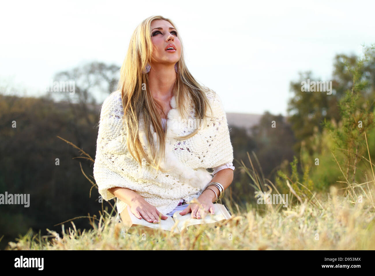 A young blond lady is sitting on her knees, kneeling and praying with ...