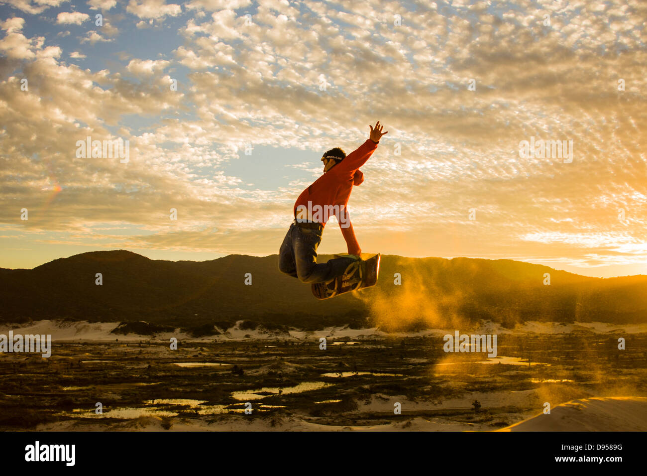 Sandboarder jumping and holding his board on the dunes of Joaquina ...