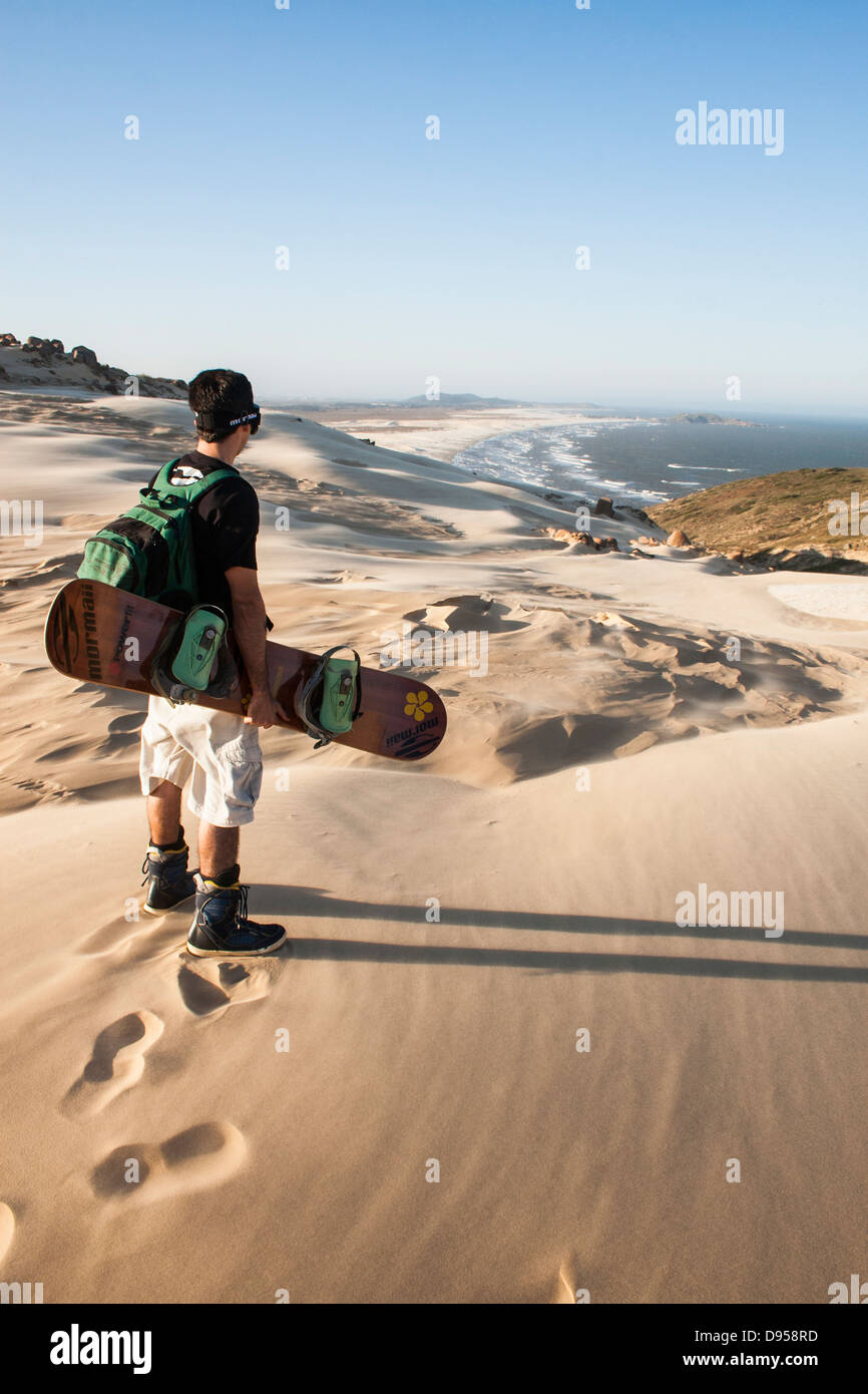 Rear view of a young man holding a sandboard and looking out at the ...