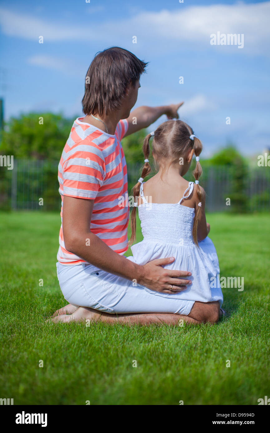 Back view of father with his daughter sitting in the yard outdoors ...