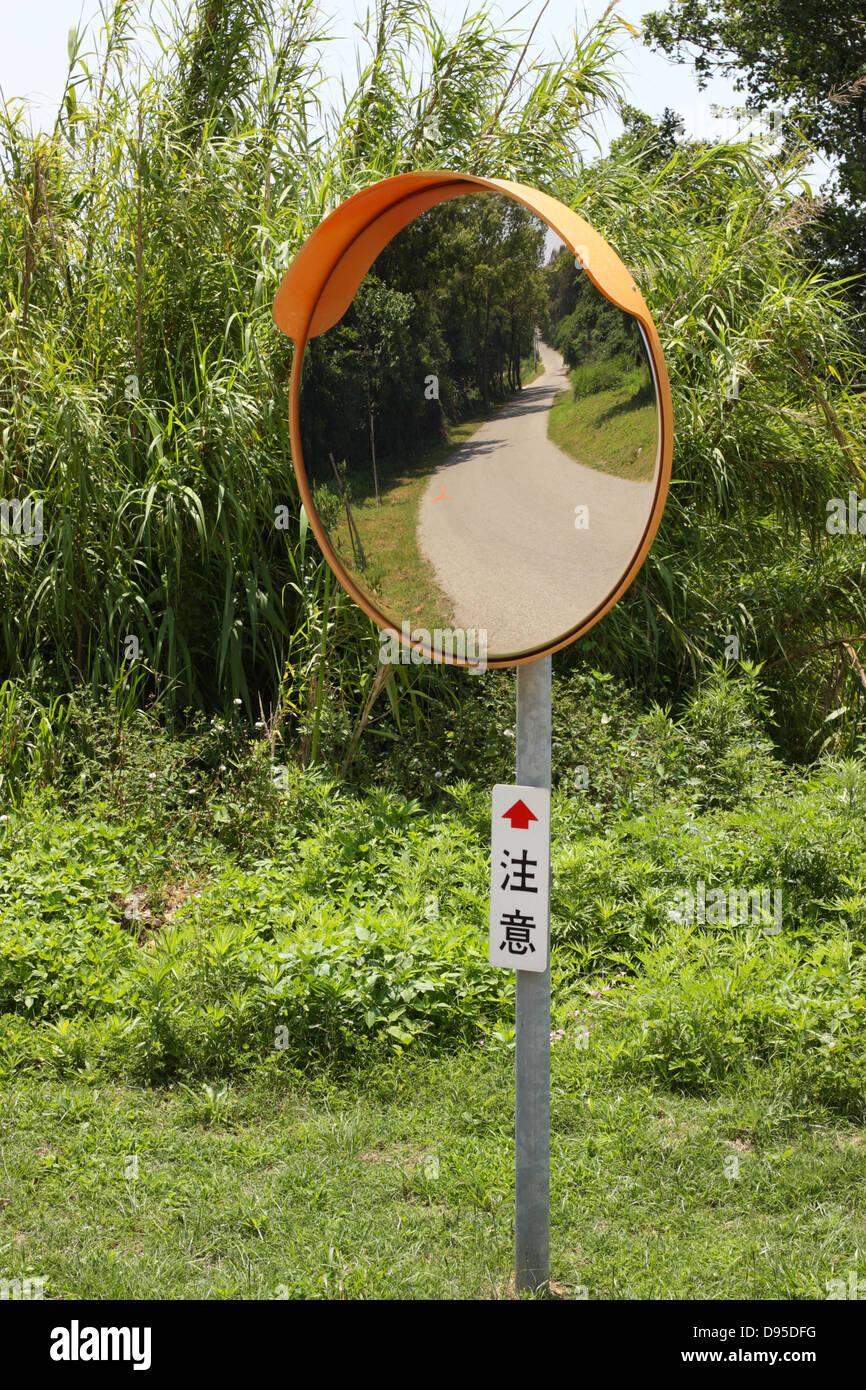 A traffic mirror on a small country road with a bike route marker on ...