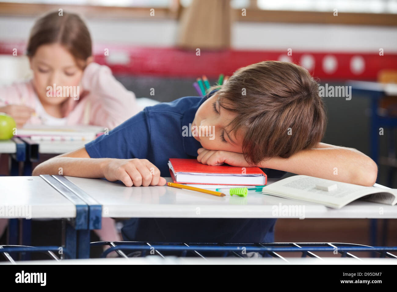 Elementary boy sleeping while girl studying in background at classroom ...