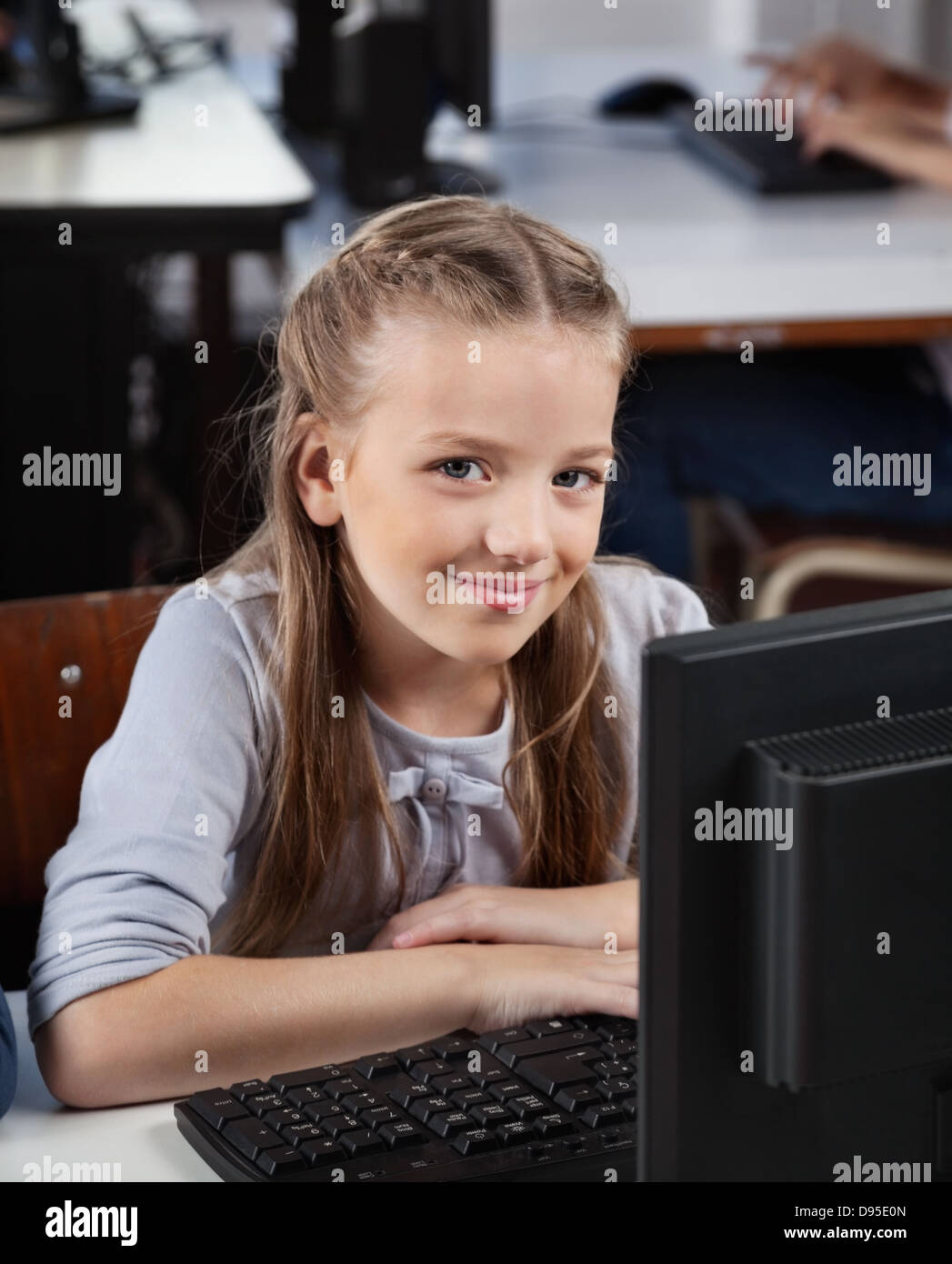 Portrait of cute schoolgirl sitting with computer at desk in lab Stock ...
