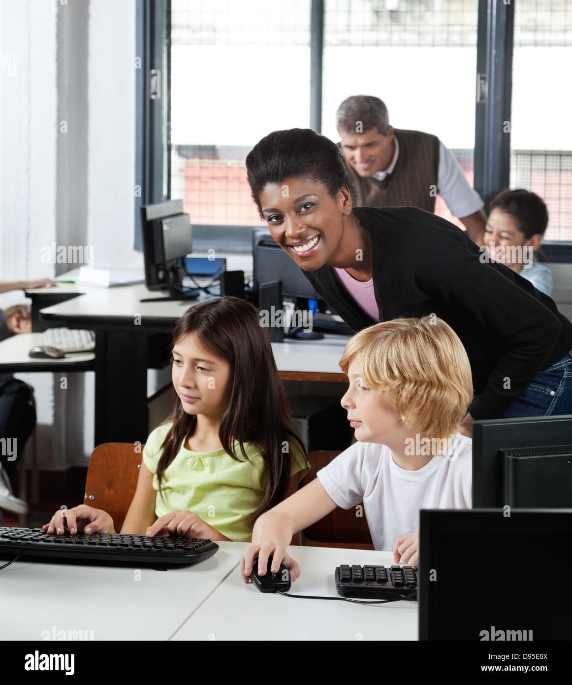 Portrait of young female teacher with students at desk in computer lab ...