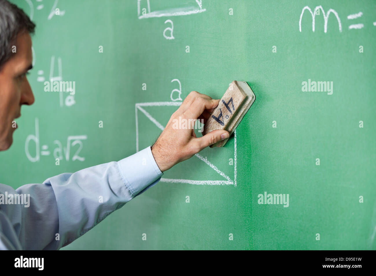Side view of mature male professor cleaning greenboard with duster in ...