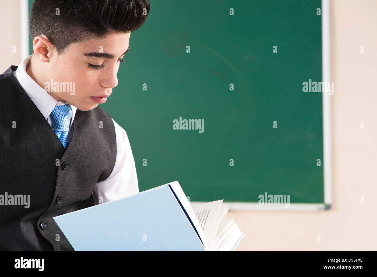 Portrait of Boy Reading Book in front of Chalkboard in Classroom Stock ...