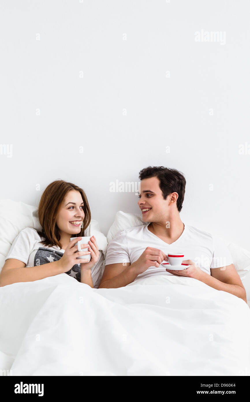 Young couple having tea in bed, smiling Stock Photo - Alamy