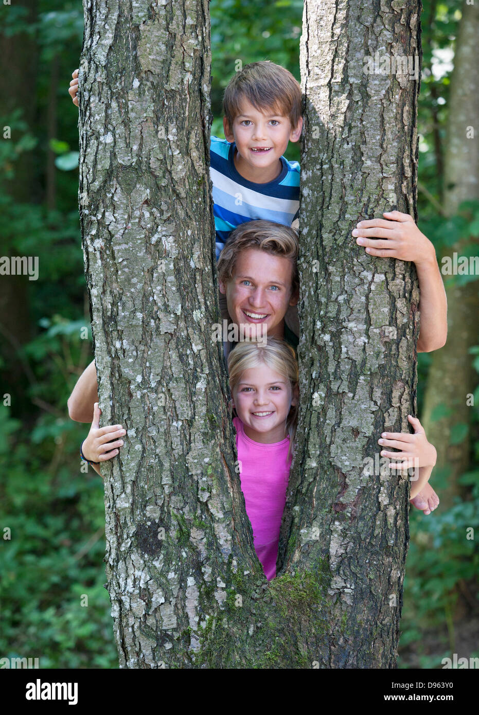 Austria, Portrait of friends standing behind tree trunk, smiling Stock ...