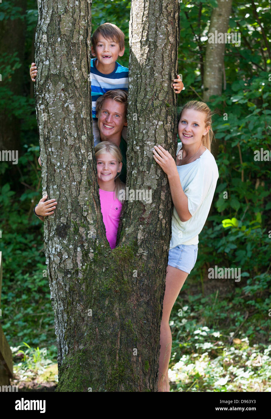 Austria, Portrait of friends standing behind tree trunk, smiling Stock ...