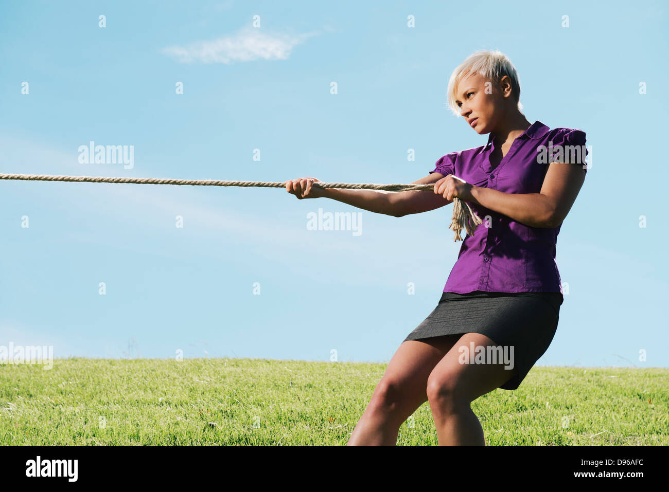 resolute business woman pulling rope against blue sky, symbol of power ...