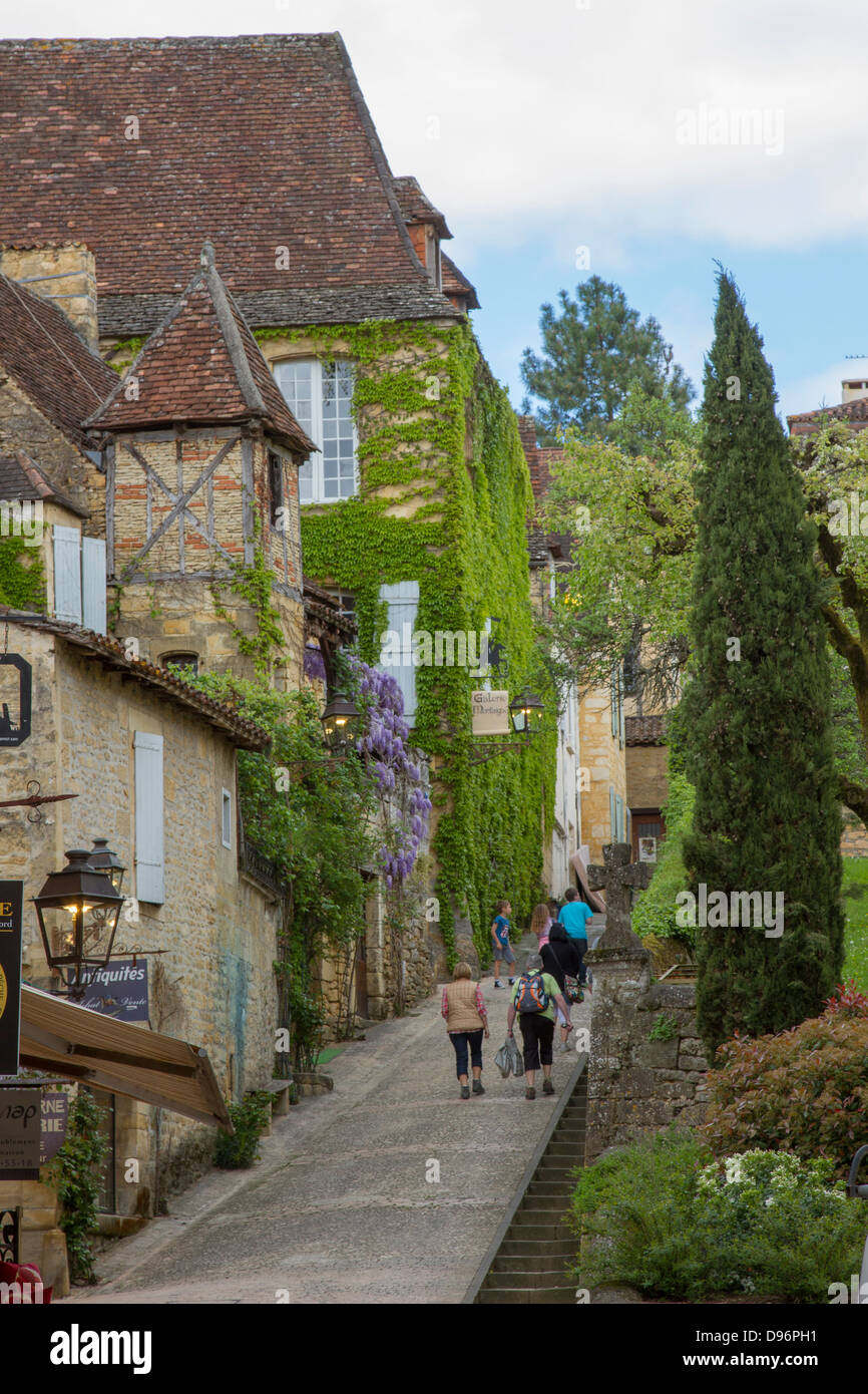 Tourists walk up charming narrow cobblestone sloped street lined with ...