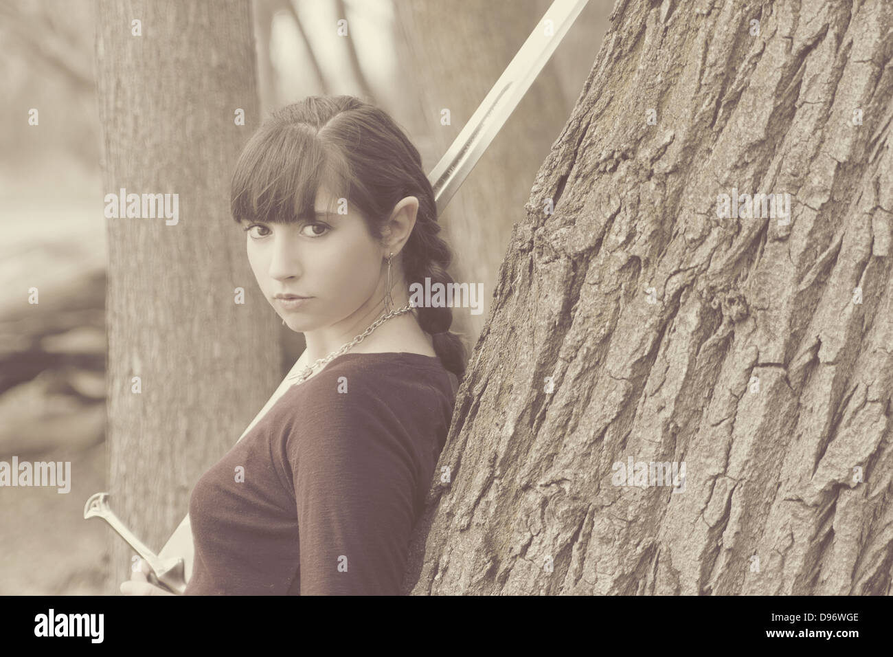Beautiful young woman with broadsword and hair in braid leans against ...