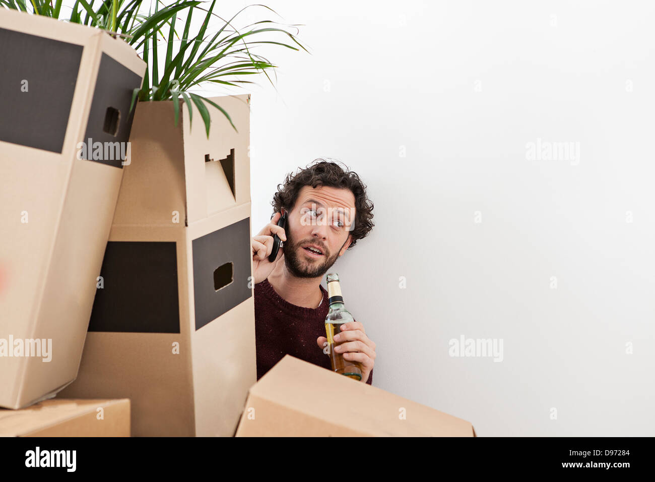 Man sitting behind stack of cardboard boxes and talking on mobile phone ...