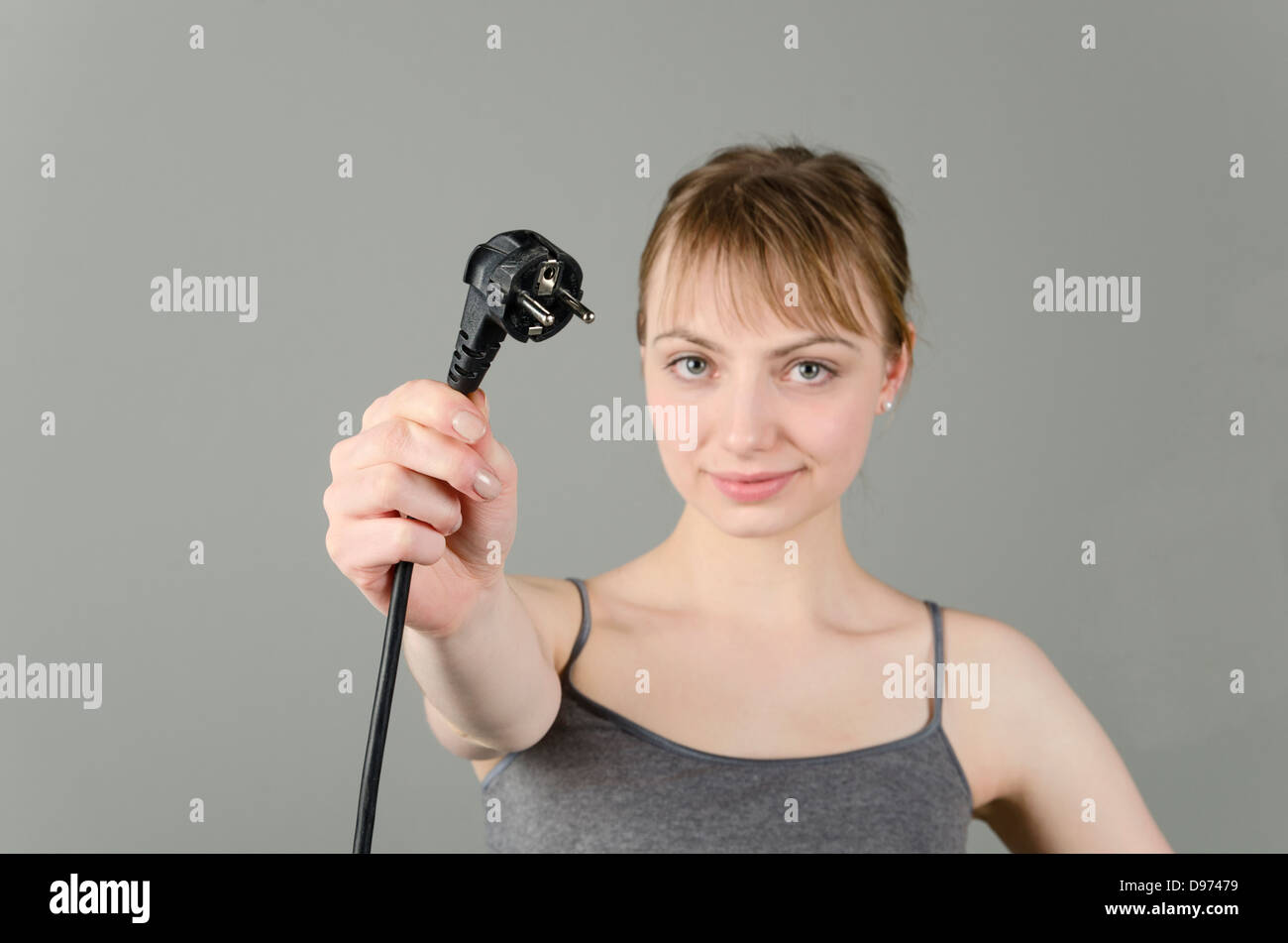 Portrait of young woman holding power plug against grey background ...