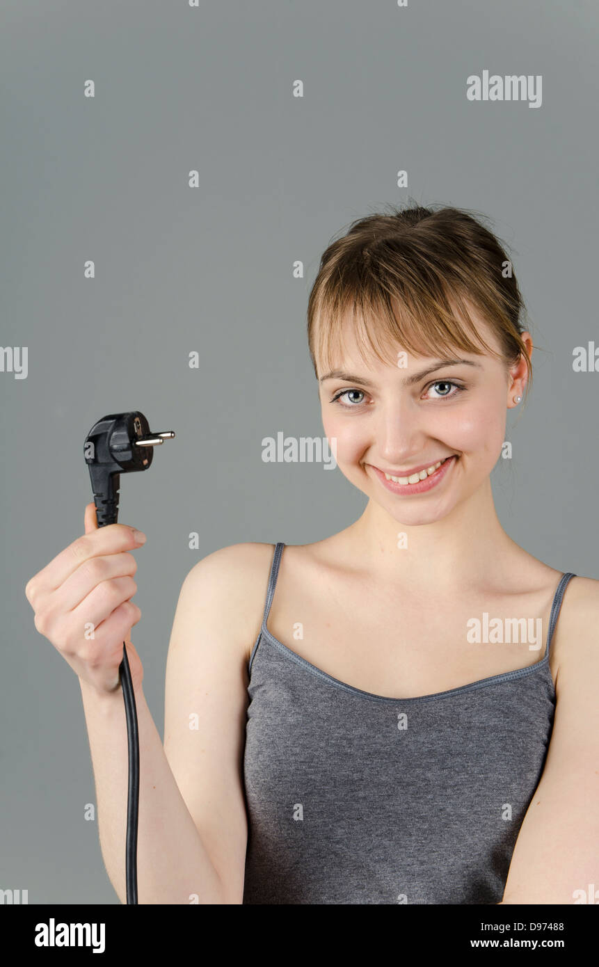 Portrait of young woman holding power plug against grey background ...