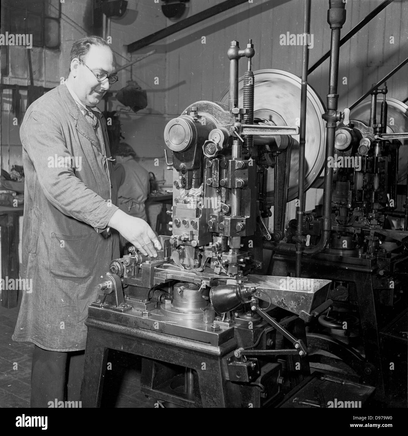 Historical 1950s. An engineer wearing a factory overall checks his ...