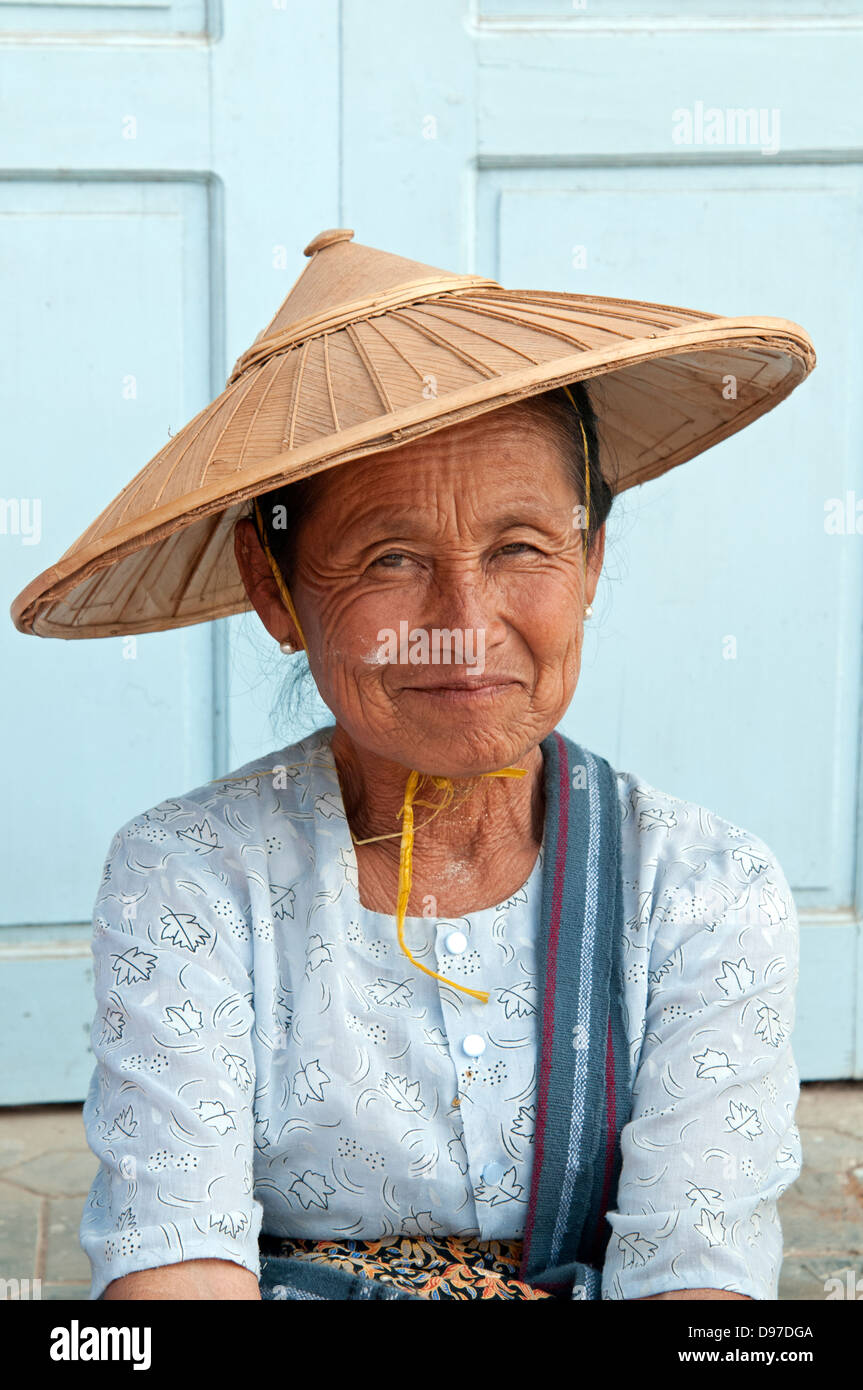 Woman wearing traditional Shan states hat sitting by blue wooden door ...