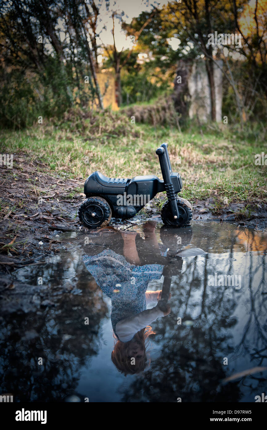 Small black plastic toddler scooter standing next to a puddle with only ...