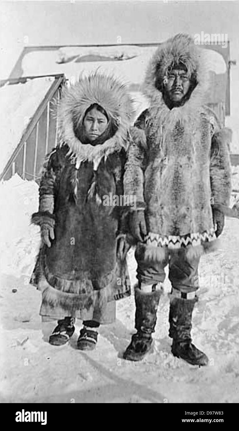 An Eskimo couple, dressed in traditional fur parkas and mukluks, stand ...