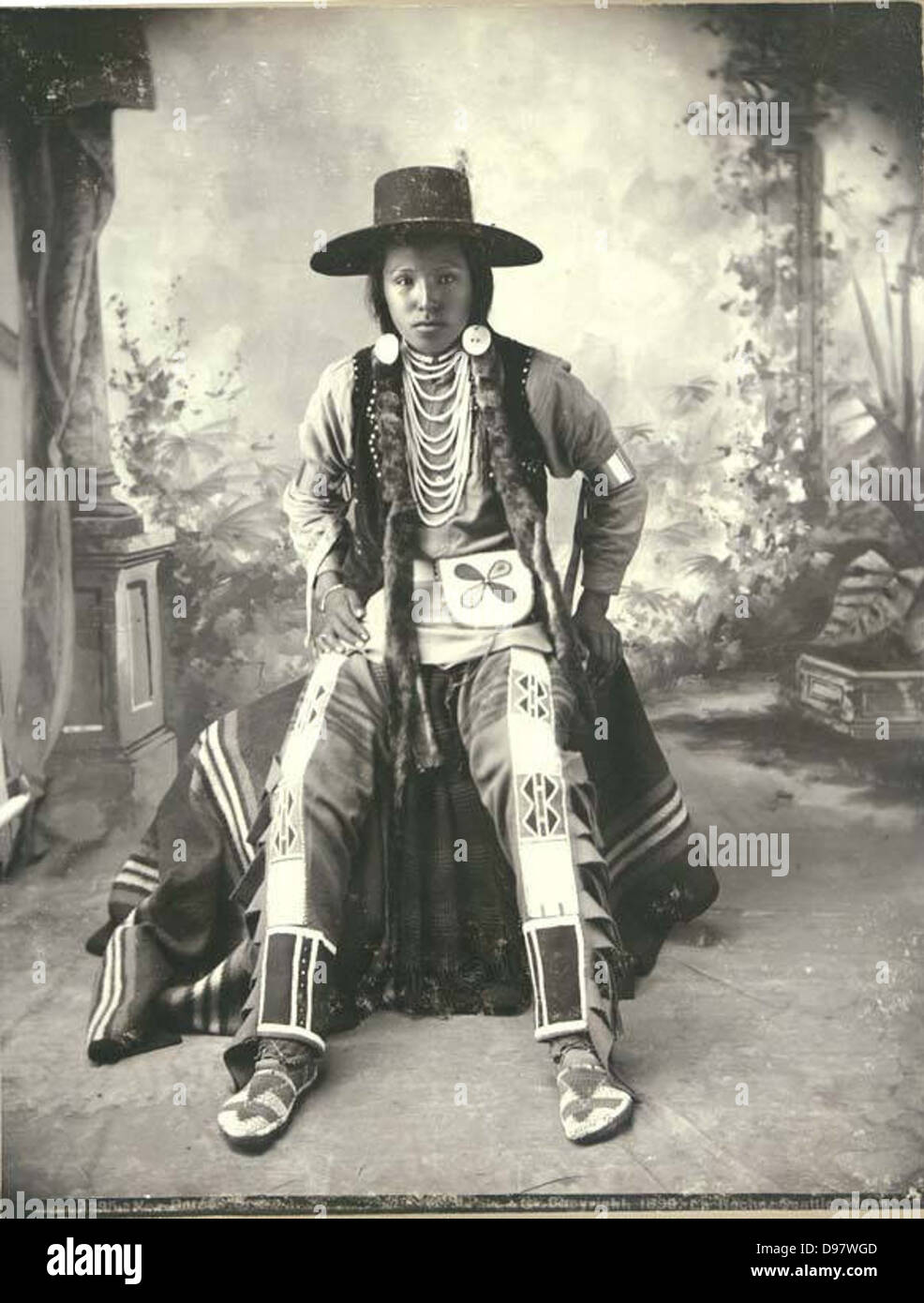 This studio portrait depicts a Nez Perce man wearing traditional beaded costumes and hats ...