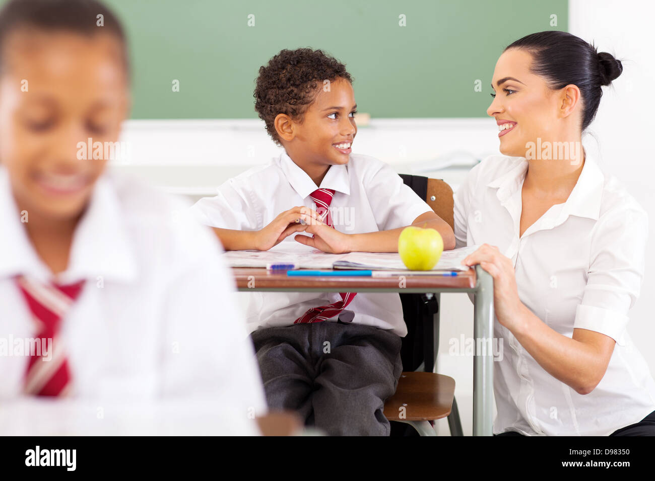 caring elementary school teacher talking to a student in classroom ...
