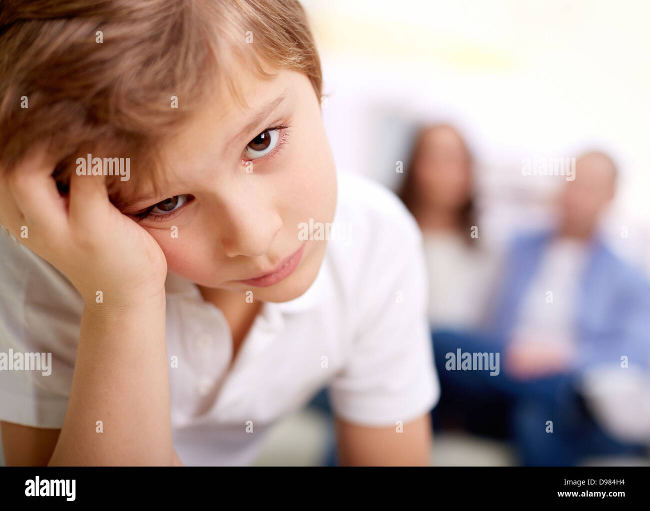 Portrait of sad boy looking at camera on background of his parents ...