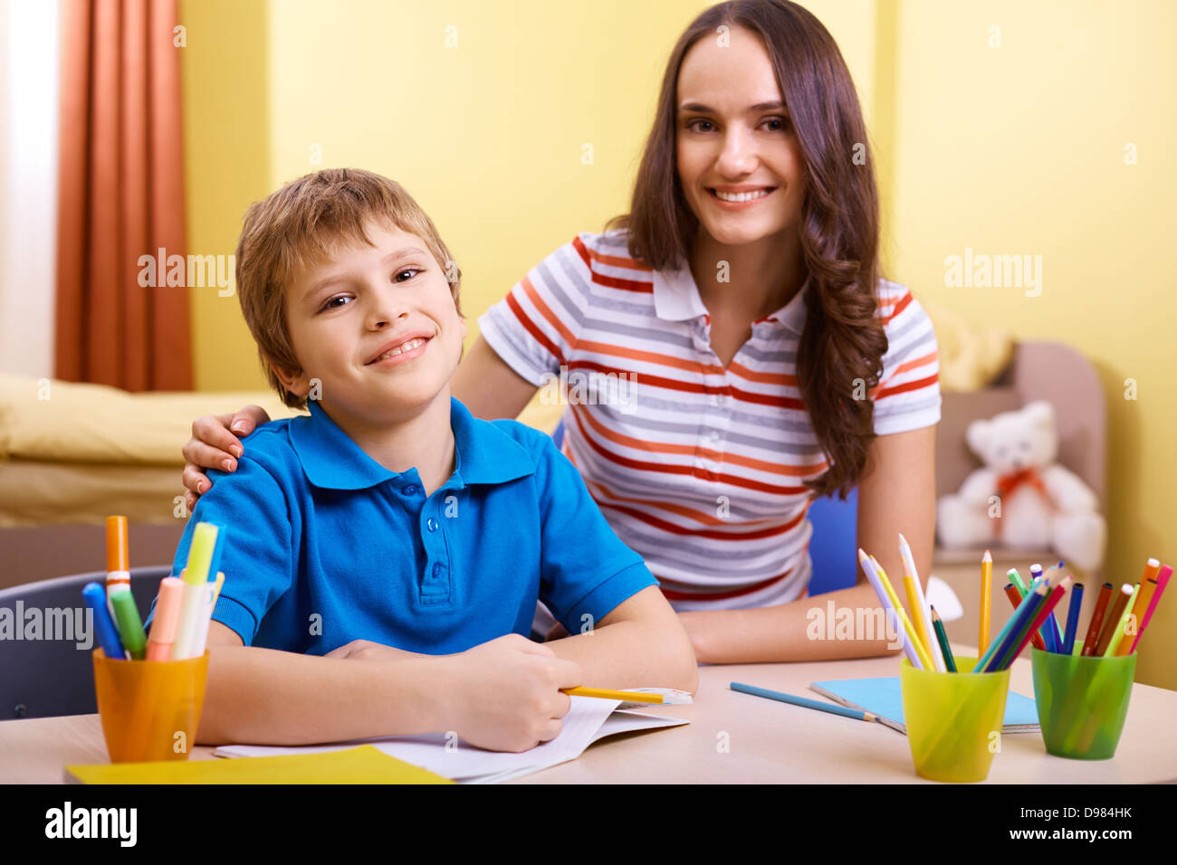 Portrait of cute schoolboy and his mother making schoolwork at home ...