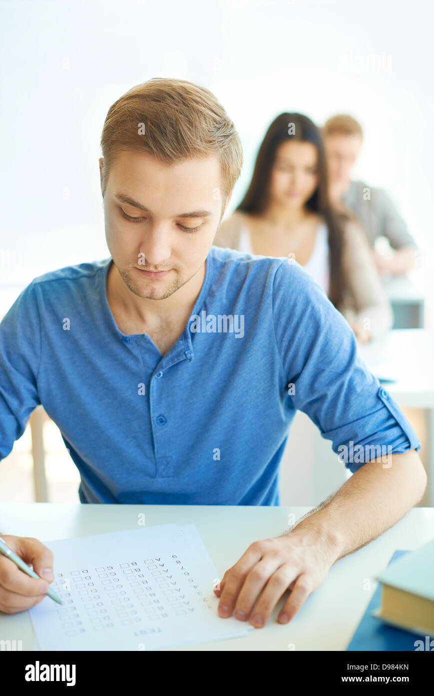 Portrait of handsome student carrying out test at lesson with ...