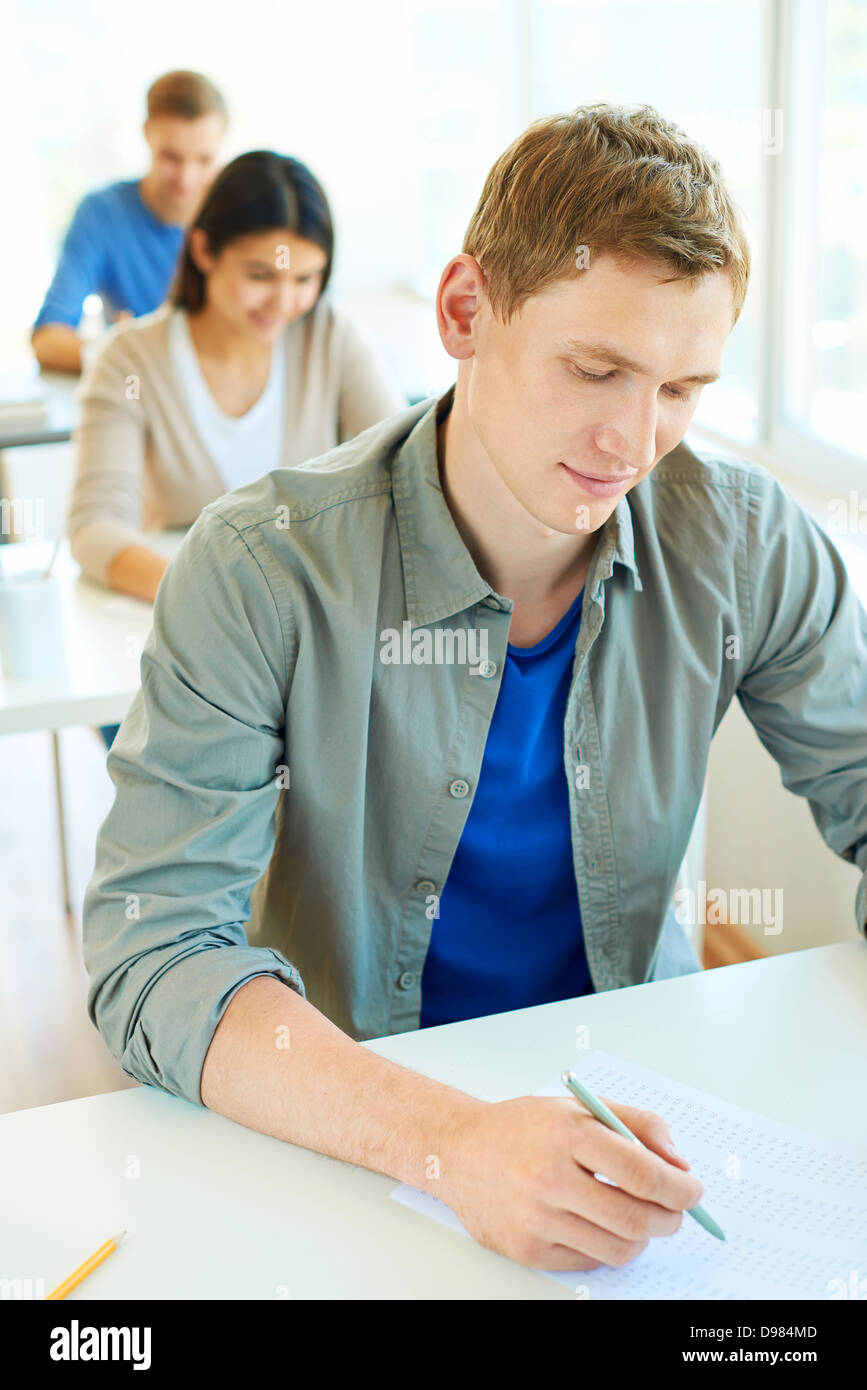 Portrait of handsome student carrying out test at lesson with ...