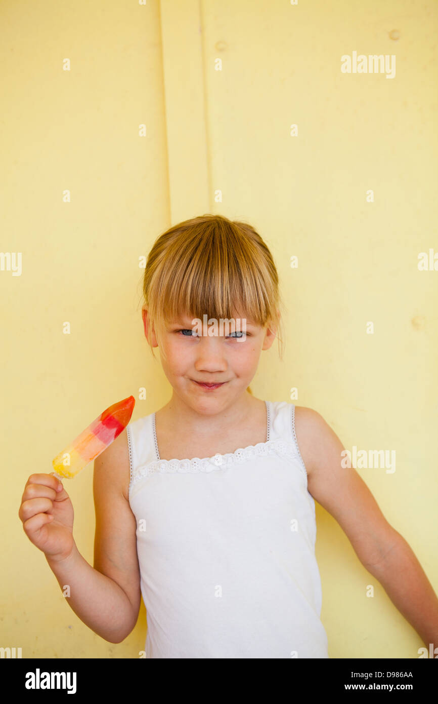 Smiling young girl with multicolored popsicle against yellow colored ...
