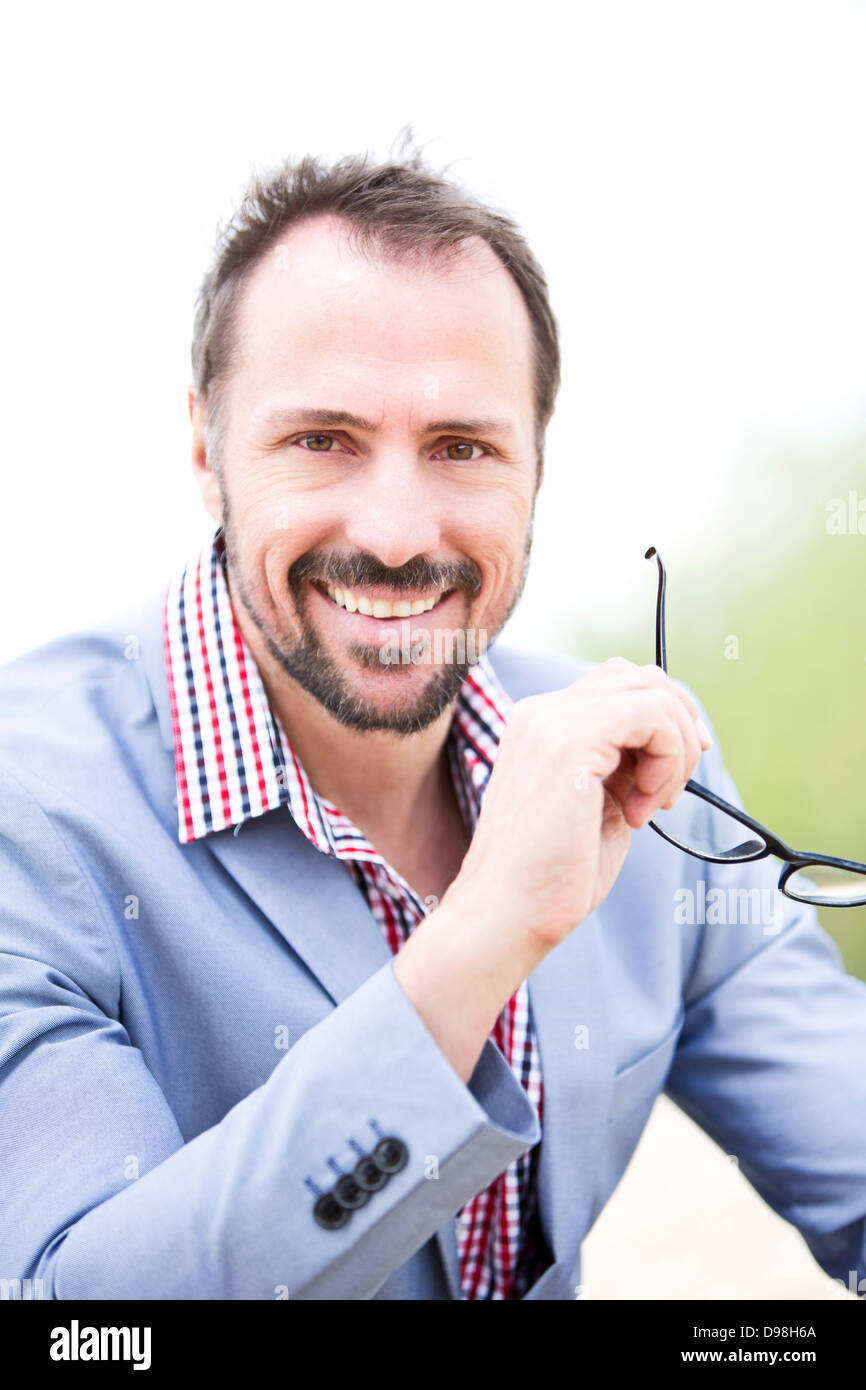 Germany, Bavaria, Portrait of businessman holding spectacles, smiling ...