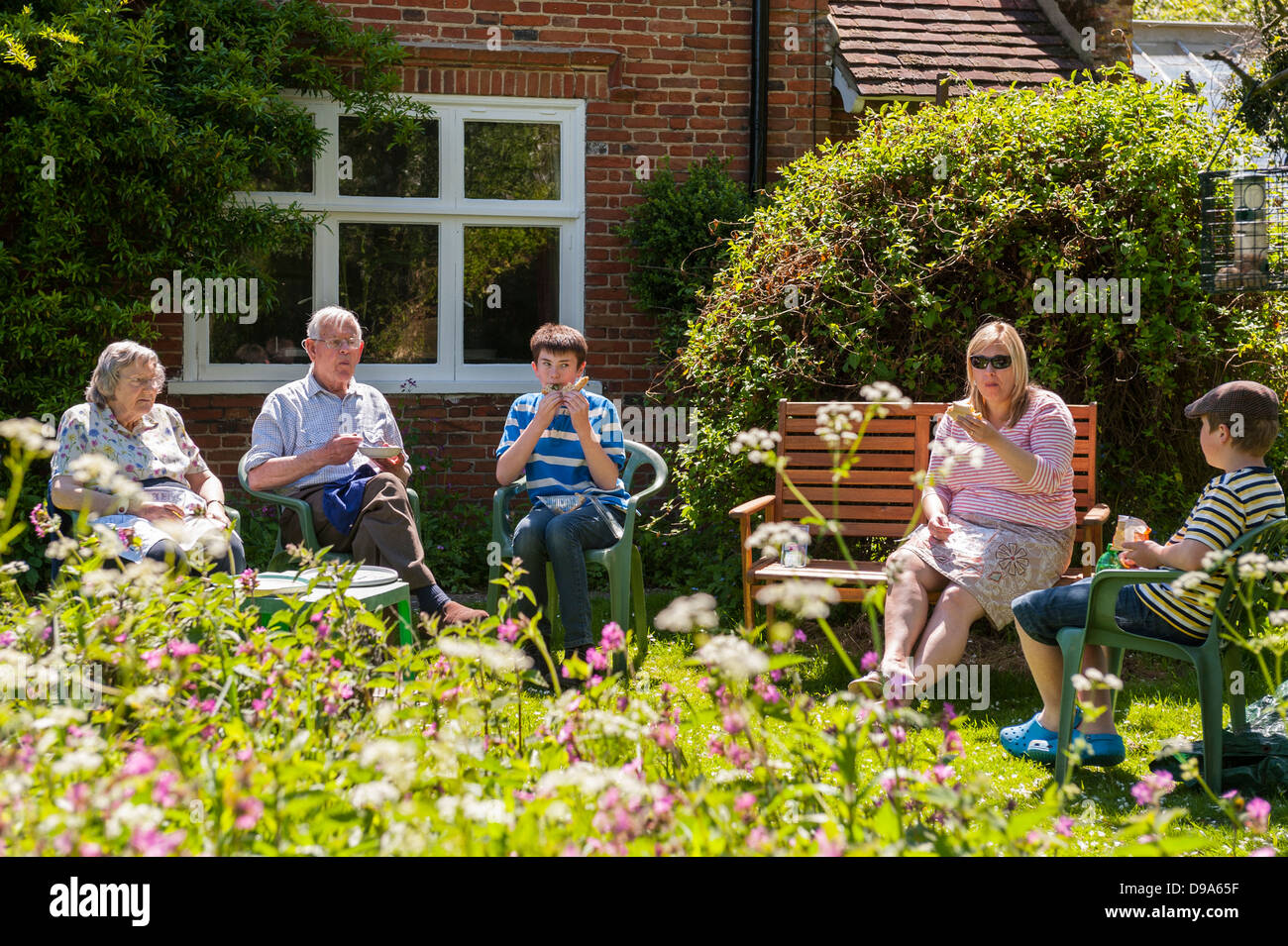 A family eating lunch outside in a cottage garden in summer in the Uk ...