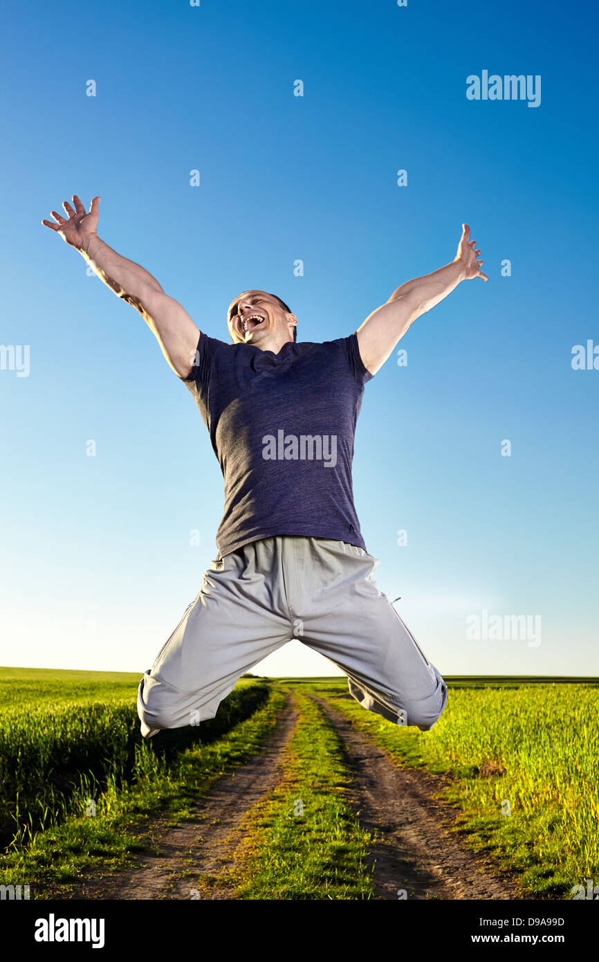 Young man jumping for joy over a rural road crossing a wheat field ...