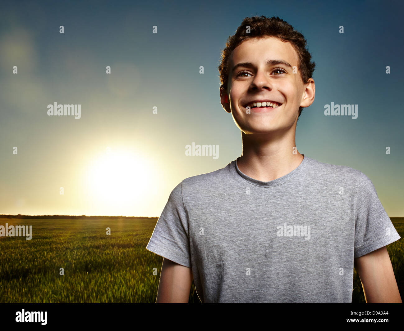 Closeup of a teenage boy with the sun behind him at sunset, in a wheat ...