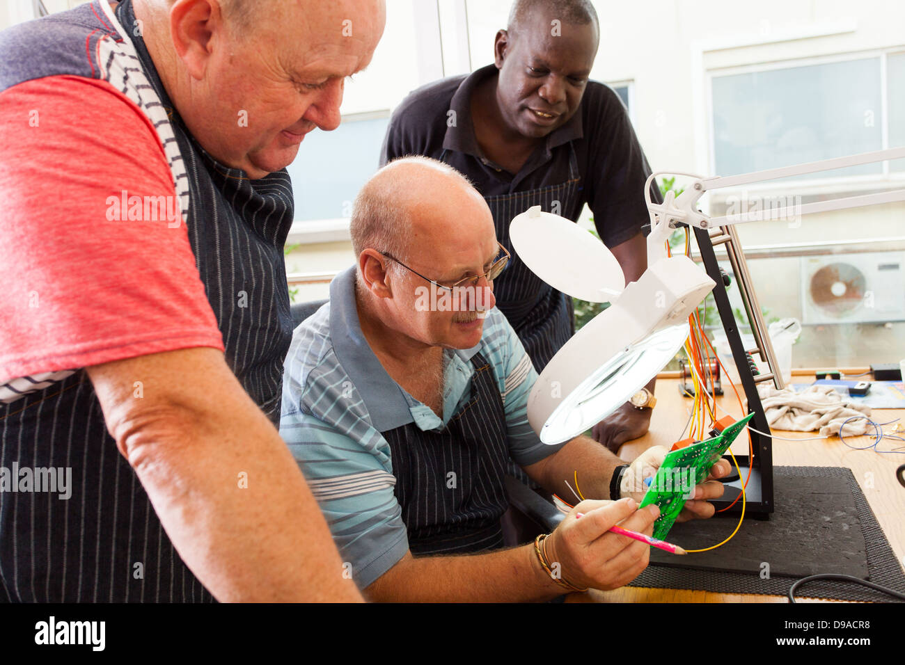 group of senior casual electrical technicians examining a circuit board ...