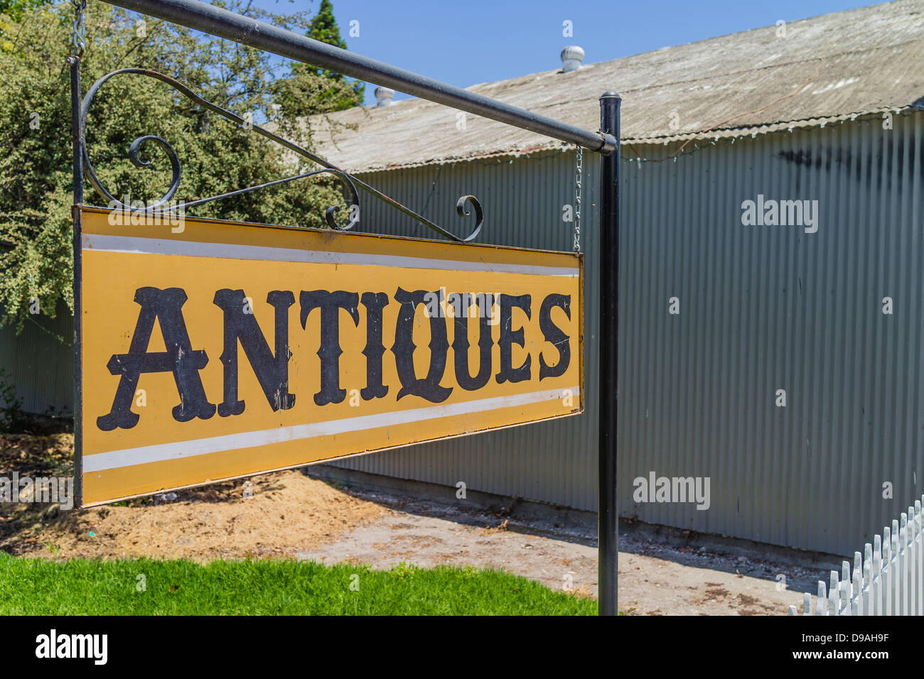 A metal sign with the lettering "Antiques" in front of a old house that ...