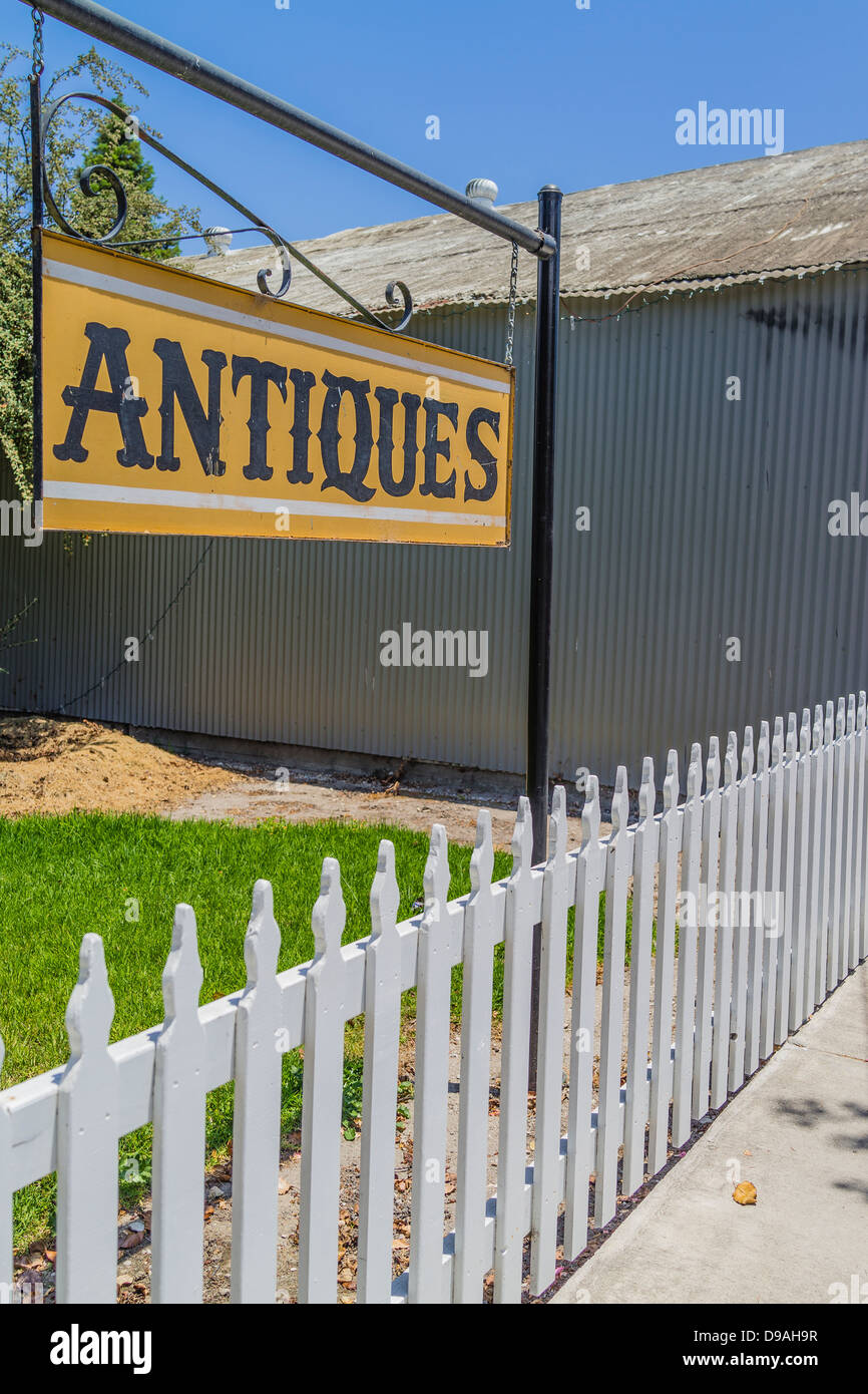 A metal sign with the lettering "Antiques" in front of a old house that ...