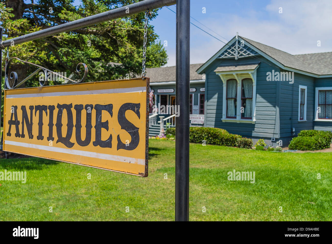 A metal sign with the lettering "Antiques" in front of a old house that ...