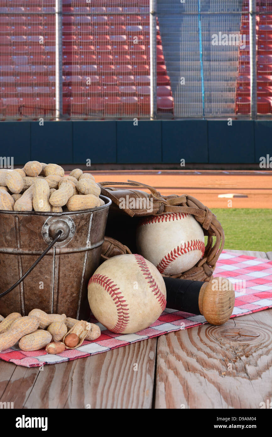 A bucket of peanuts and baseball equipment on a wood picnic table with ...