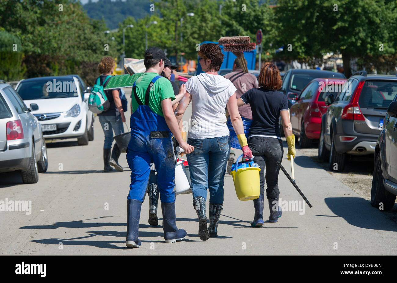Numerous volunteer helpers walk along a street with shovels and brooms ...