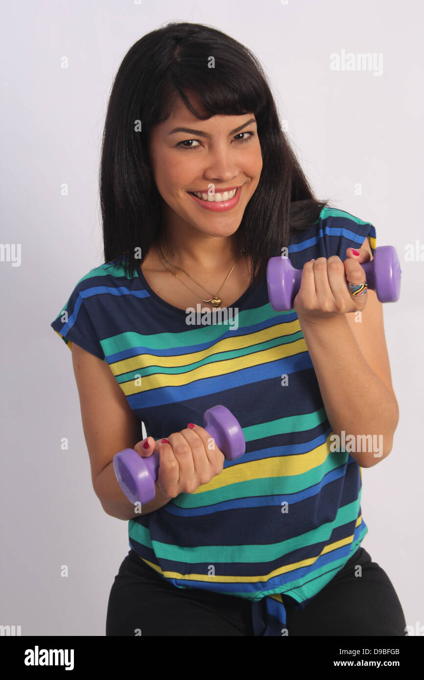 Lovely young woman with a beautiful smile exercising with dumbbells ...