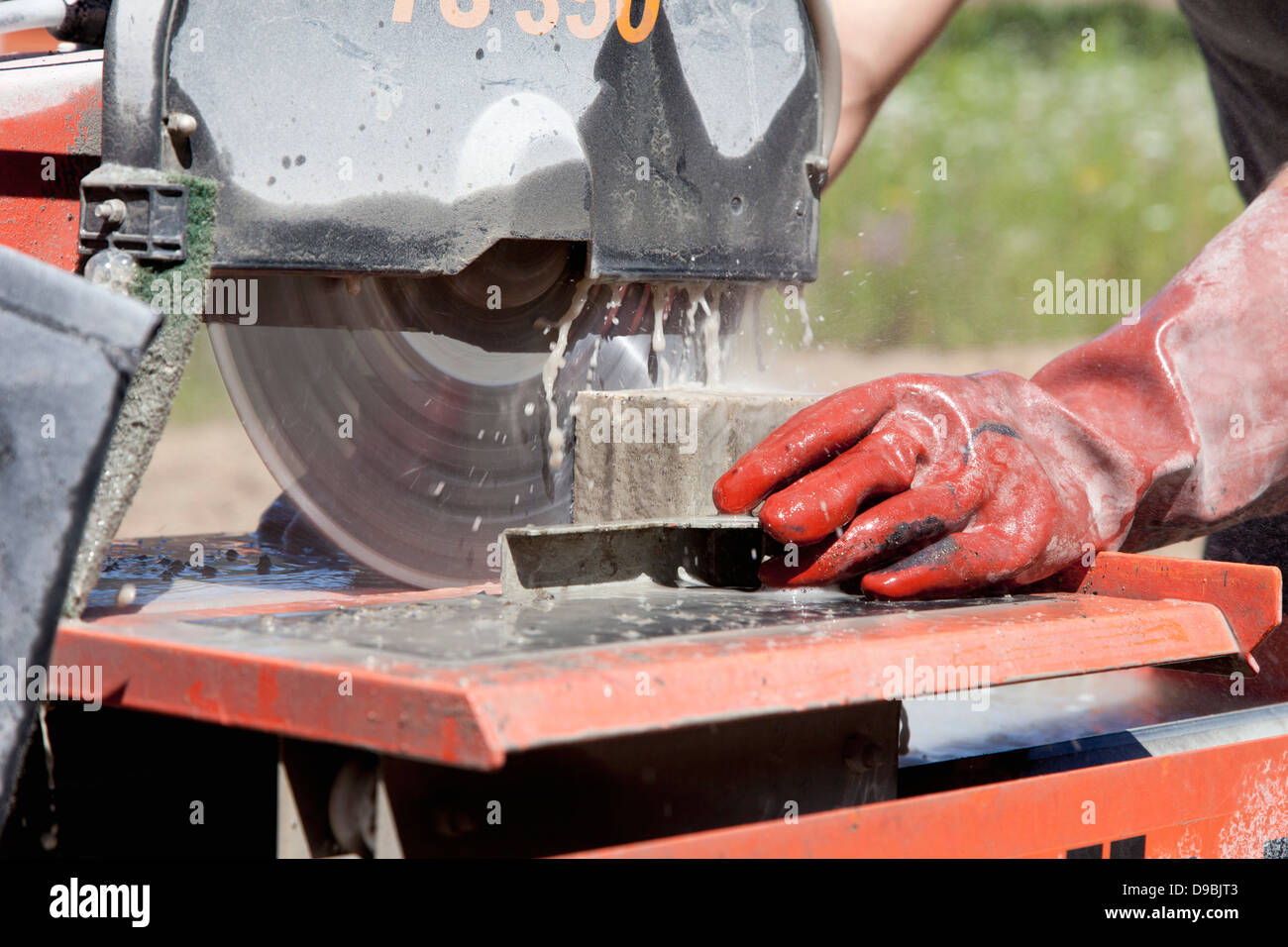 Germany, Rhineland Palatinate, Young man cutting paving stone with saw ...