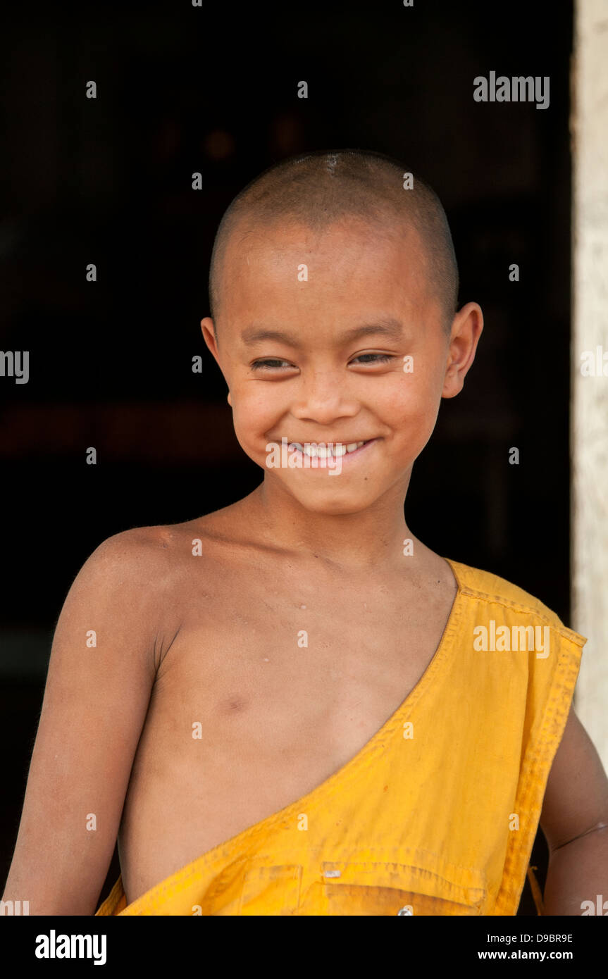Boy monk laughing in yellow robes stands in a temple doorway Myanmar ...